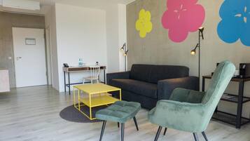 Uma sala de estar moderna com um sofá, uma poltrona verde, uma mesa de centro amarela e uma escrivaninha com cadeira.