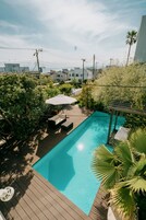 Piscina retangular com deck de madeira, rodeada por vegetação e uma pérgula.