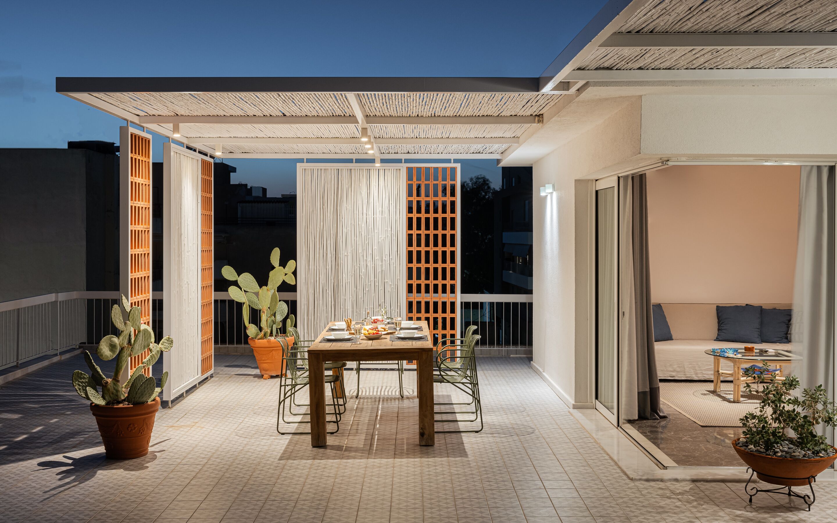 Pátio externo com mesa posta para refeições, rodeado por plantas em vasos e um design arquitetônico moderno.