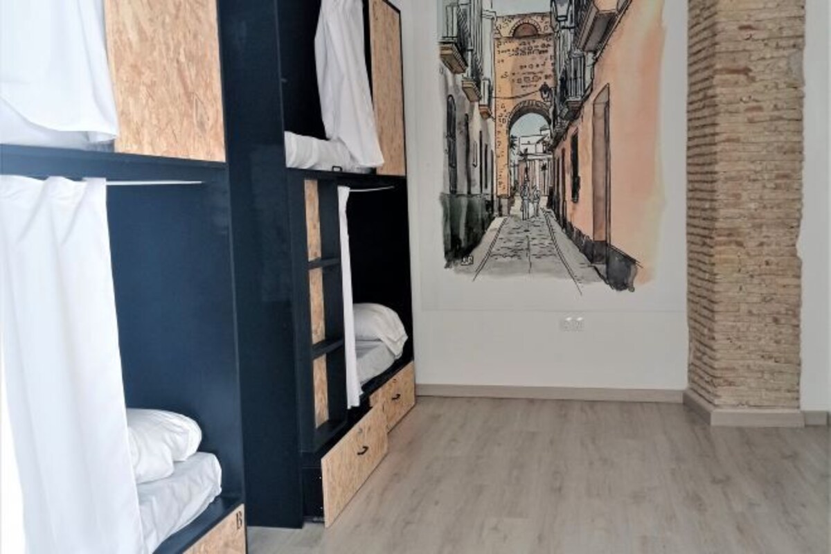 Quarto com beliches, um mural com uma cena de rua e uma parede de tijolos.