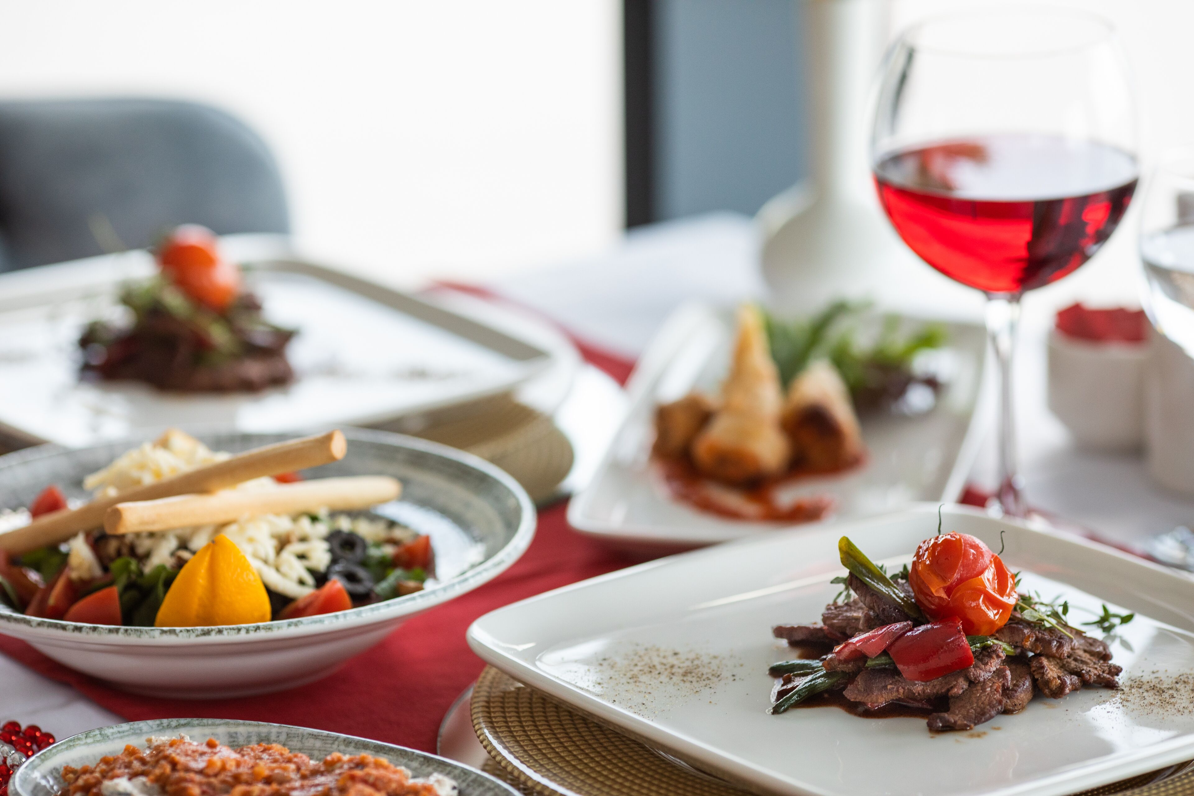 Uma mesa de jantar com diversos pratos, incluindo uma salada, um bife e uma taça de vinho tinto.