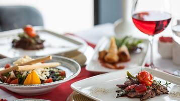 Uma mesa de jantar com diversos pratos, incluindo uma salada, um bife e uma taça de vinho tinto.