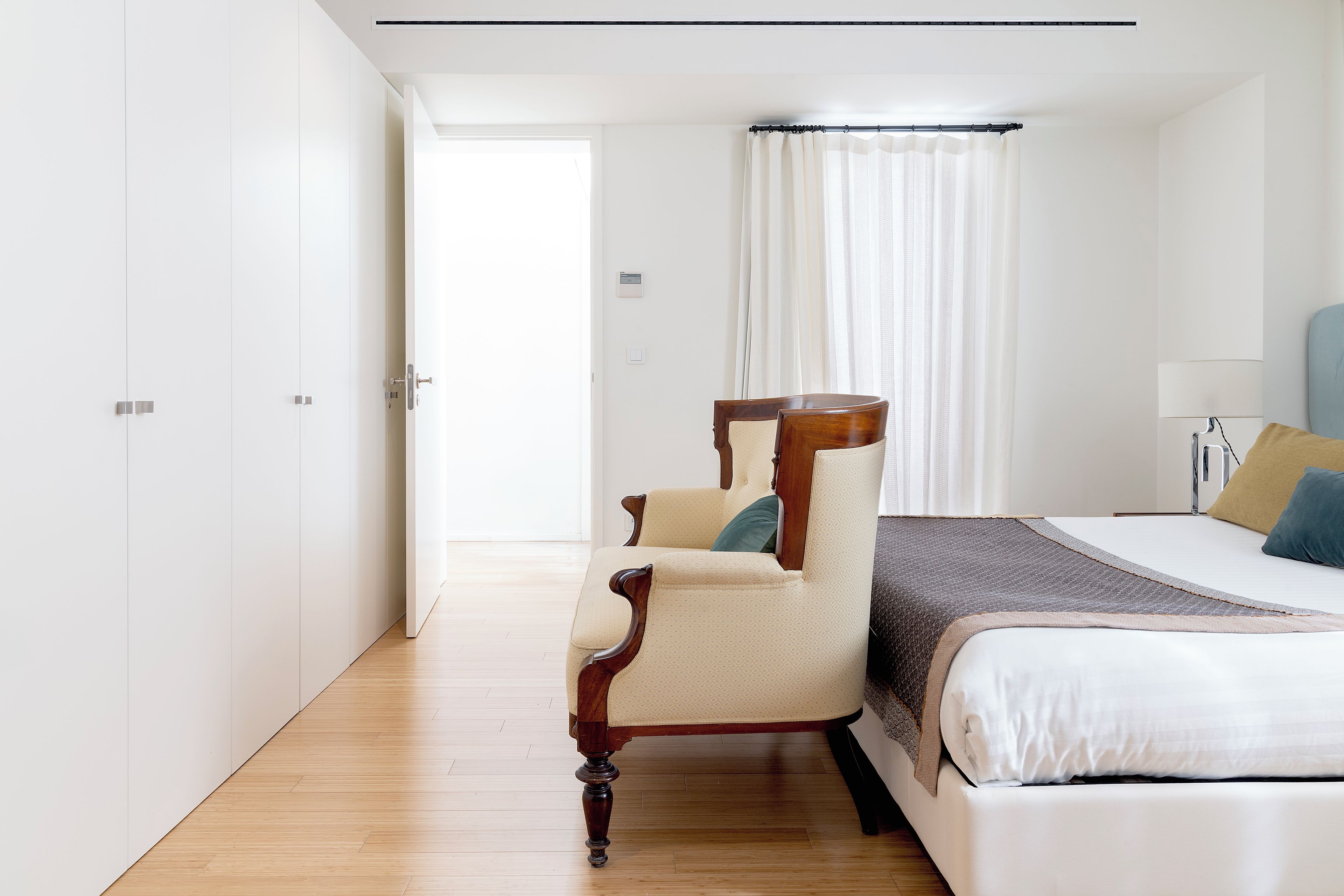 Quarto de hotel com cama, cadeira, mesa de cabeceira e janela com cortinas.