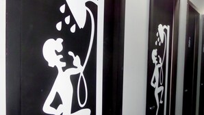 Corredor com paredes pretas e silhuetas brancas de uma pessoa utilizando um chuveiro.