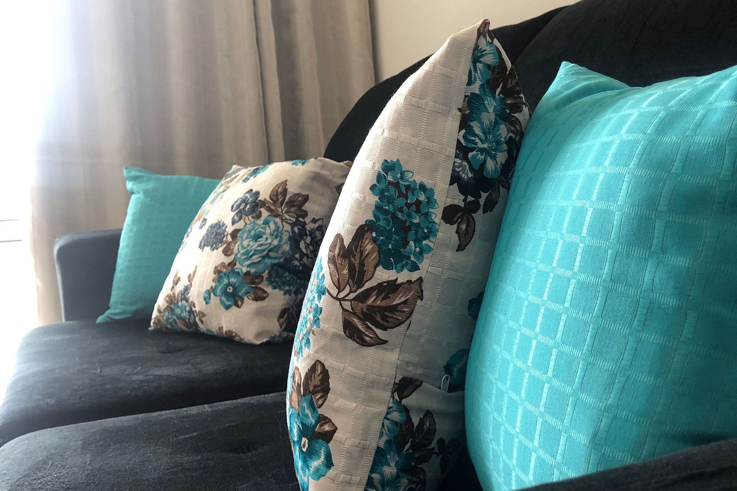 Um sofá de cor escura com duas almofadas decorativas, uma estampada com flores e outra com um padrão geométrico.