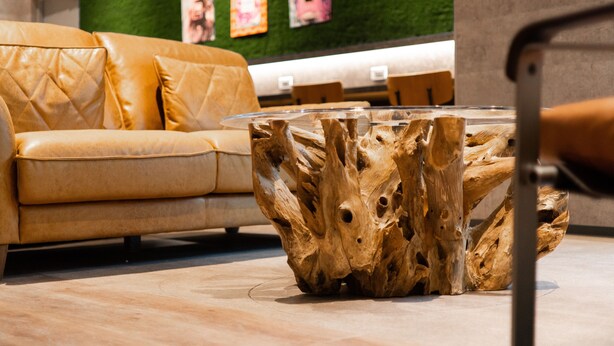 Uma sala de estar moderna com um sofá de couro, uma mesa de centro de vidro com base de madeira e uma parede verde com obras de arte emolduradas.