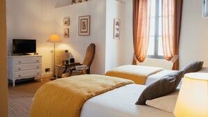 Quarto de hotel com duas camas, televisão, luminária, cadeira e quadros na parede.
