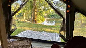 Tenda com vista para uma área gramada e um lago. No interior, há uma cadeira de vime e um tapete estampado.