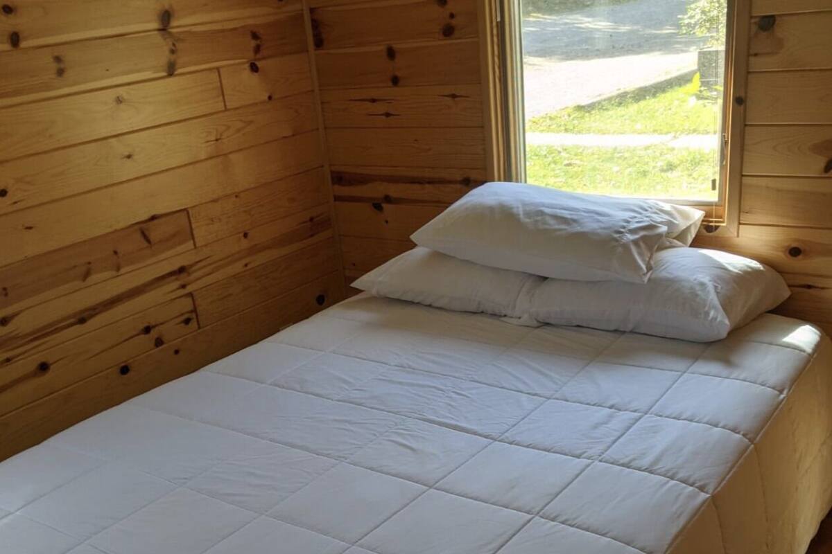 Uma cama de solteiro com roupa de cama branca num quarto de cabana de madeira.