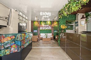 Um hall de hotel com uma mesa de recepção, um sofá e uma vitrine de vidro com petiscos.