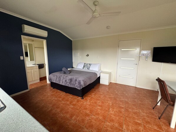 Quarto com cama, mesas de cabeceira, televisão e ventoinha no teto.