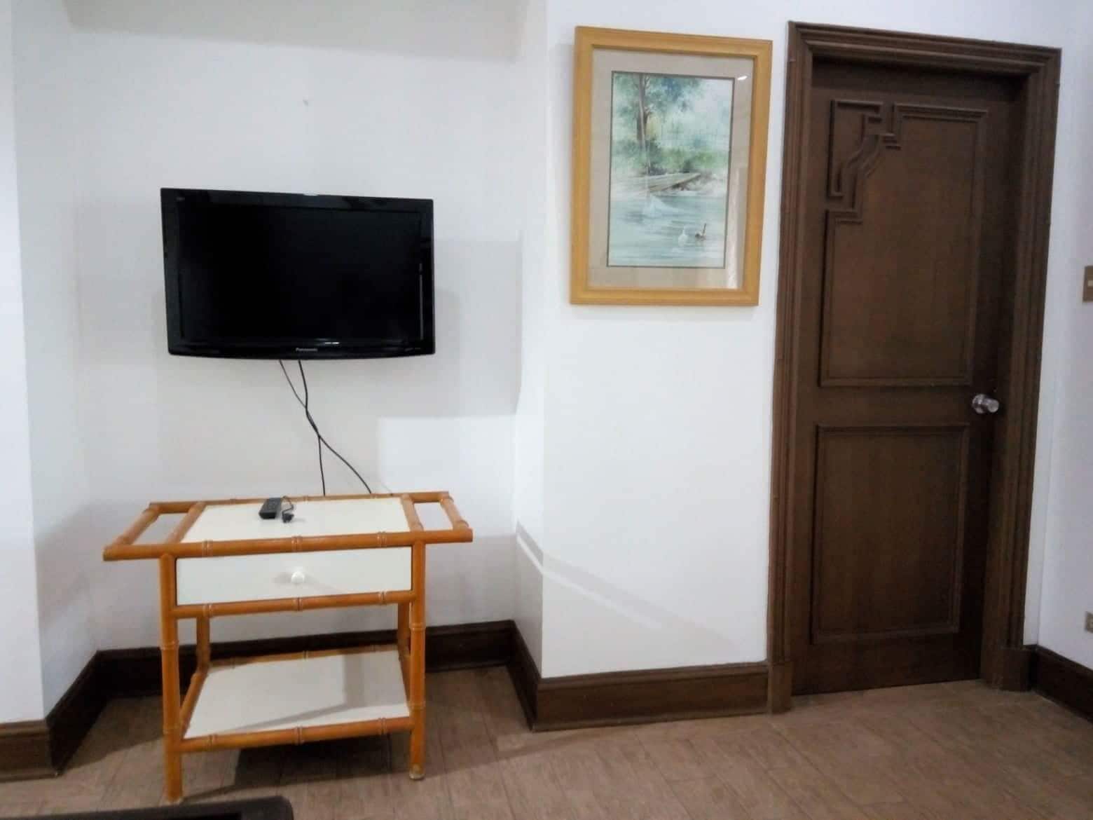 Quarto com televisão na parede, quadro emoldurado e porta de madeira.