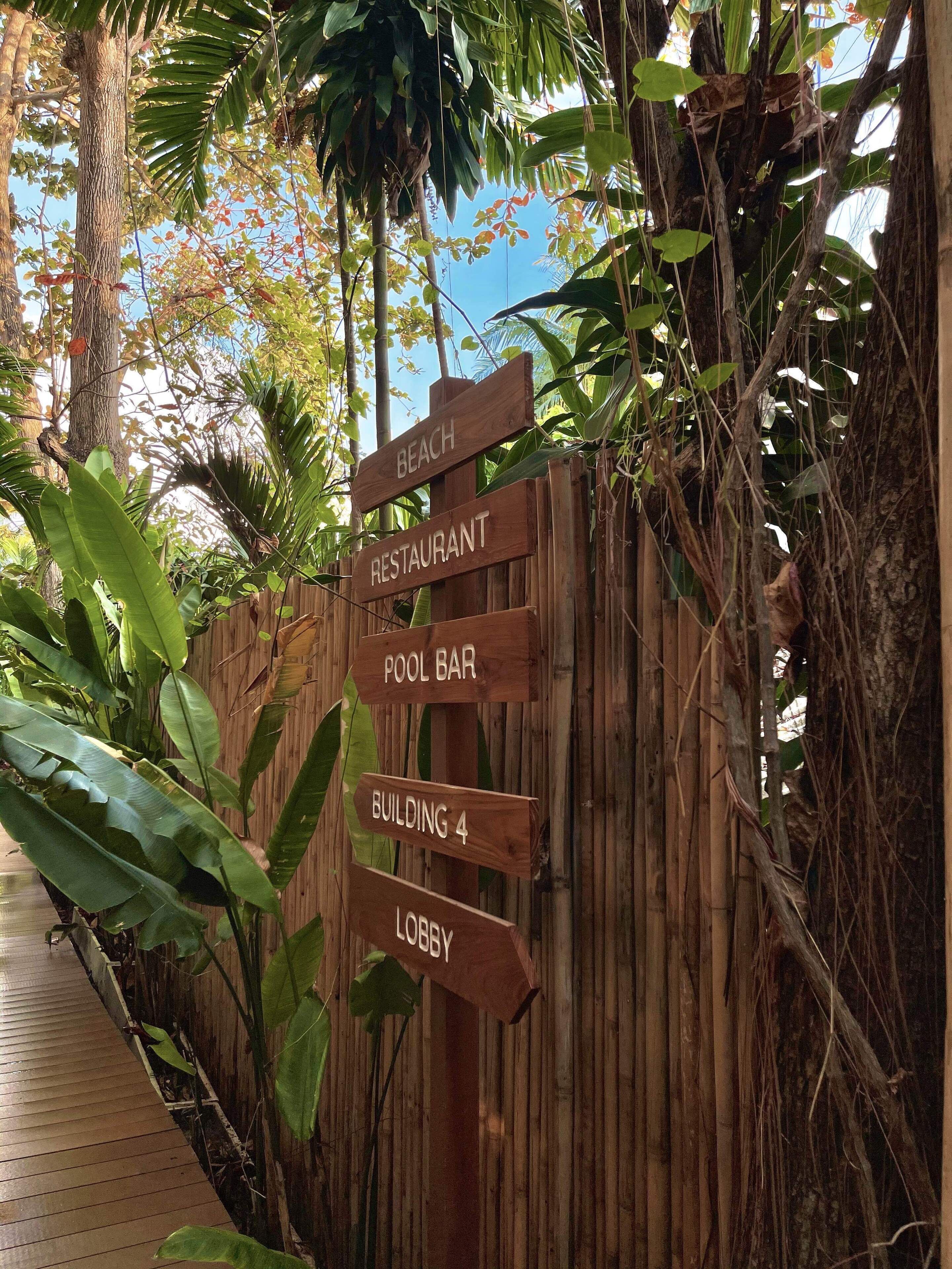 Um sinal de madeira com indicações para a praia, restaurante, bar da piscina, edifício 4 e saguão.