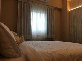 Quarto com cama, janela com cortinas leves e ar-condicionado fixado na parede.