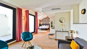 Uma sala de estar moderna com uma poltrona azul, um sofá cinzento e um espaço de jantar com mesa posta para dois.