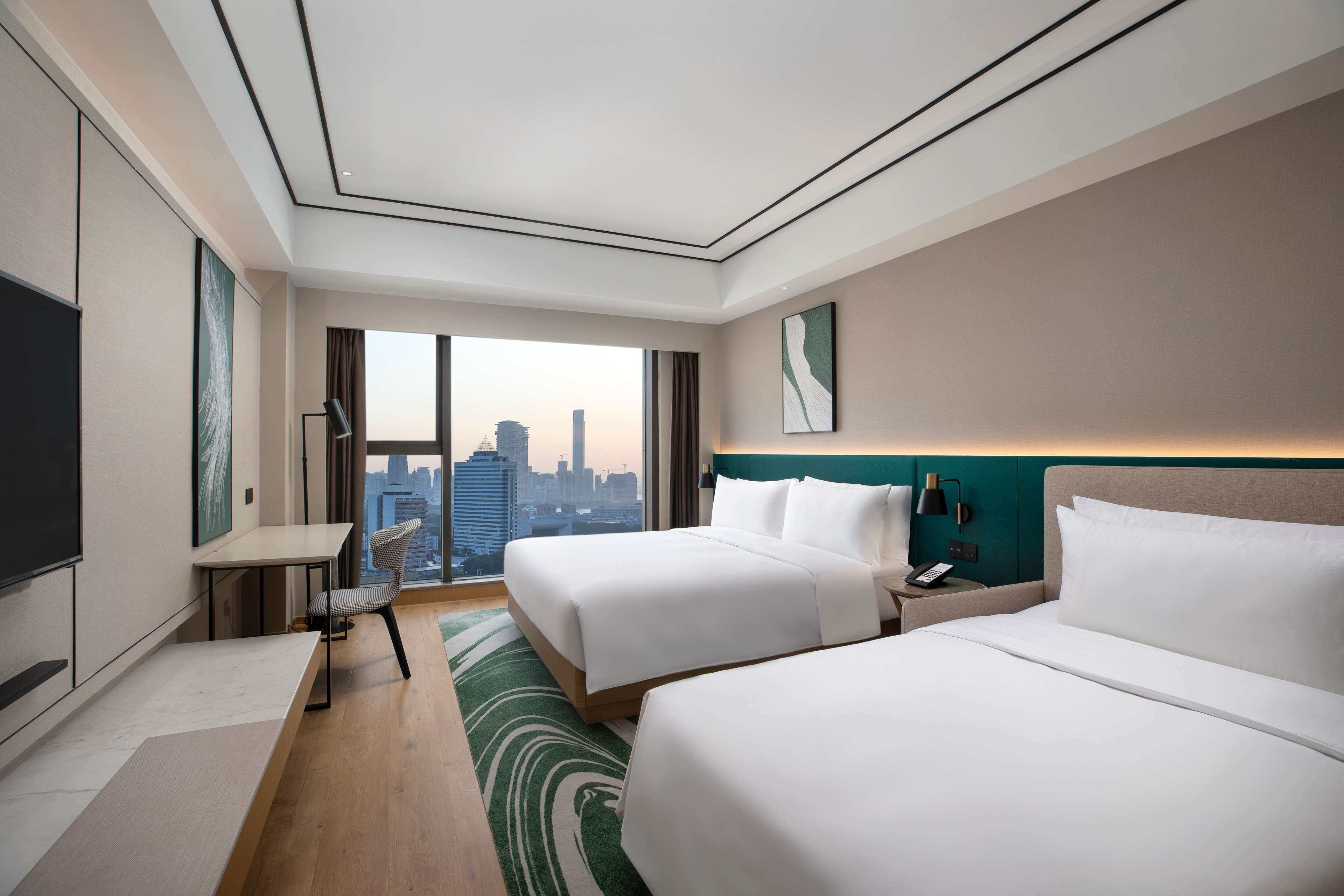 Quarto de hotel com duas camas, uma escrivaninha, uma cadeira, uma televisão e vista para a cidade.