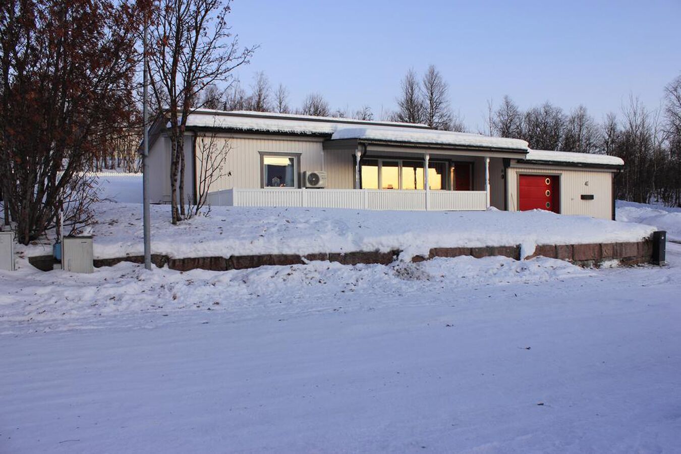 Um edifício térreo com porta vermelha, varanda coberta e paisagem coberta de neve.
