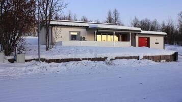 Um edifício térreo com porta vermelha, varanda coberta e paisagem coberta de neve.