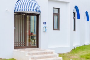 Um edifício branco com toldo listrado em azul e branco sobre a entrada, uma pequena placa azul e uma janela com moldura marrom.