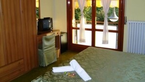 Quarto de hotel com cama, escrivaninha, computador, cadeira e janela com cortinas.