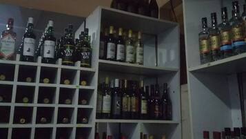 Prateleiras repletas de diversas garrafas de bebidas alcoólicas, incluindo marcas como Gilbey's Gin e Four Corners.