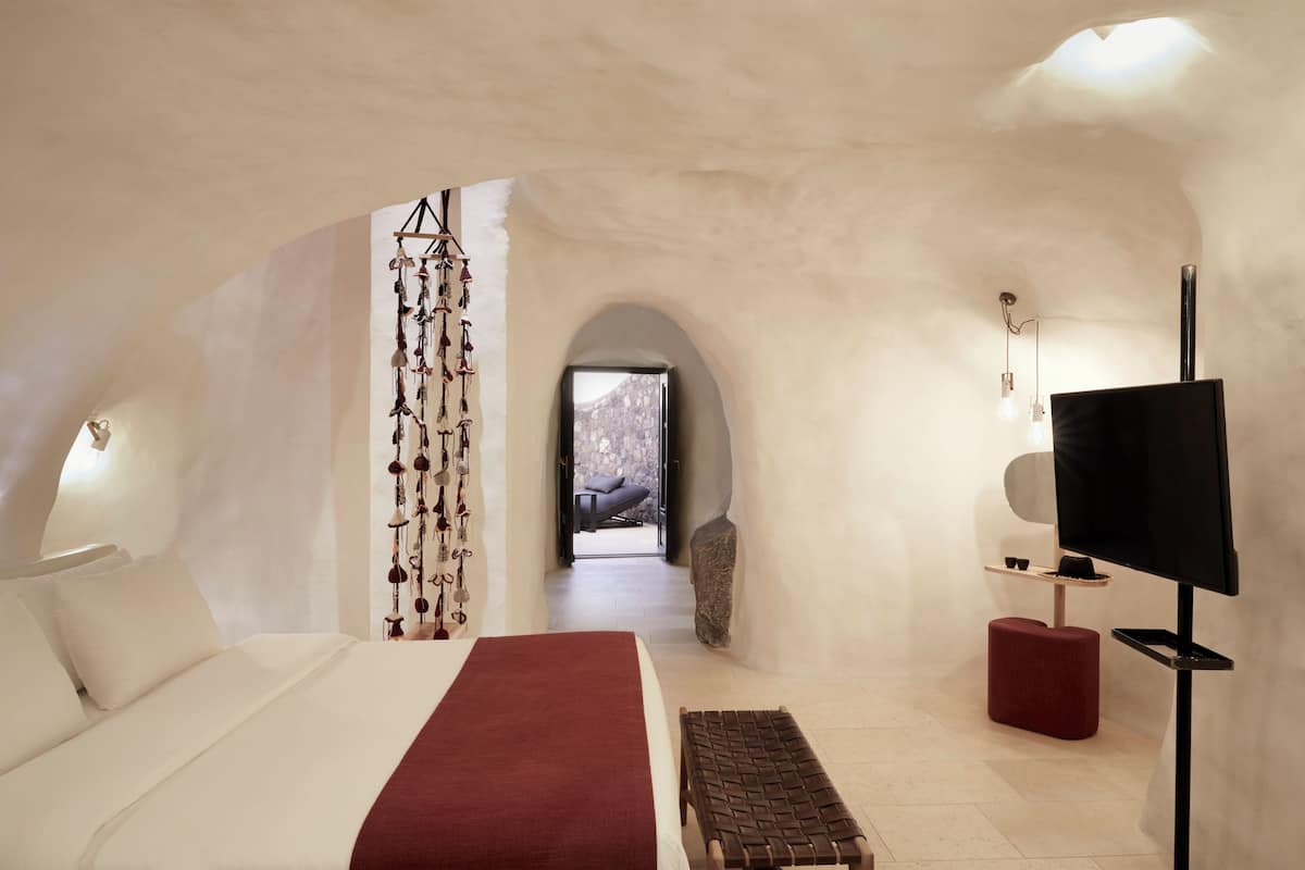 Um quarto moderno com uma cama, um banco vermelho, uma televisão e uma parede de pedra.