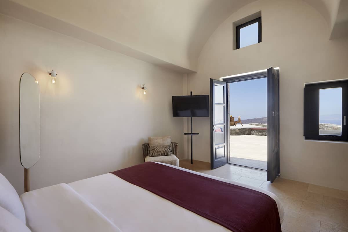 Quarto com cama, poltrona, televisão e uma janela grande.