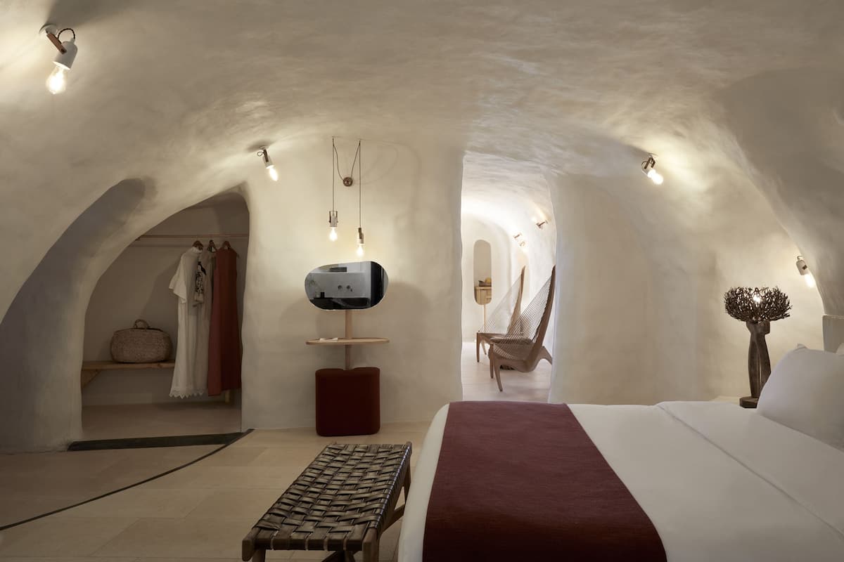 Um quarto aconchegante com arco, com uma cama, um banco, uma TV e uma cadeira.