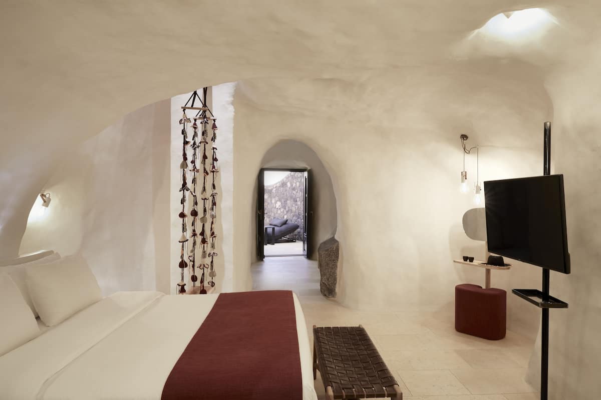 Um quarto moderno com uma cama, um banco vermelho, uma televisão e uma parede de pedra.