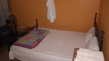 Uma cama de solteiro com lençol branco e colcha colorida, cabeceira de madeira e dossel branco.