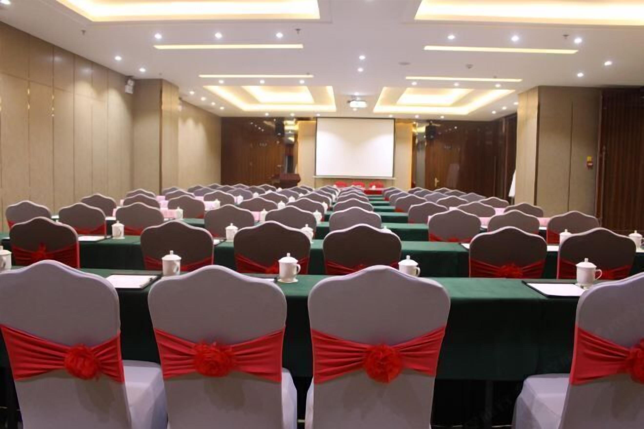 Uma sala de conferências com fileiras de mesas e cadeiras, cada uma com um laço vermelho nas costas das cadeiras.