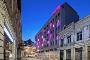 Um hotel de vários andares com fachada moderna, grandes janelas e um letreiro de neon destacado no topo.