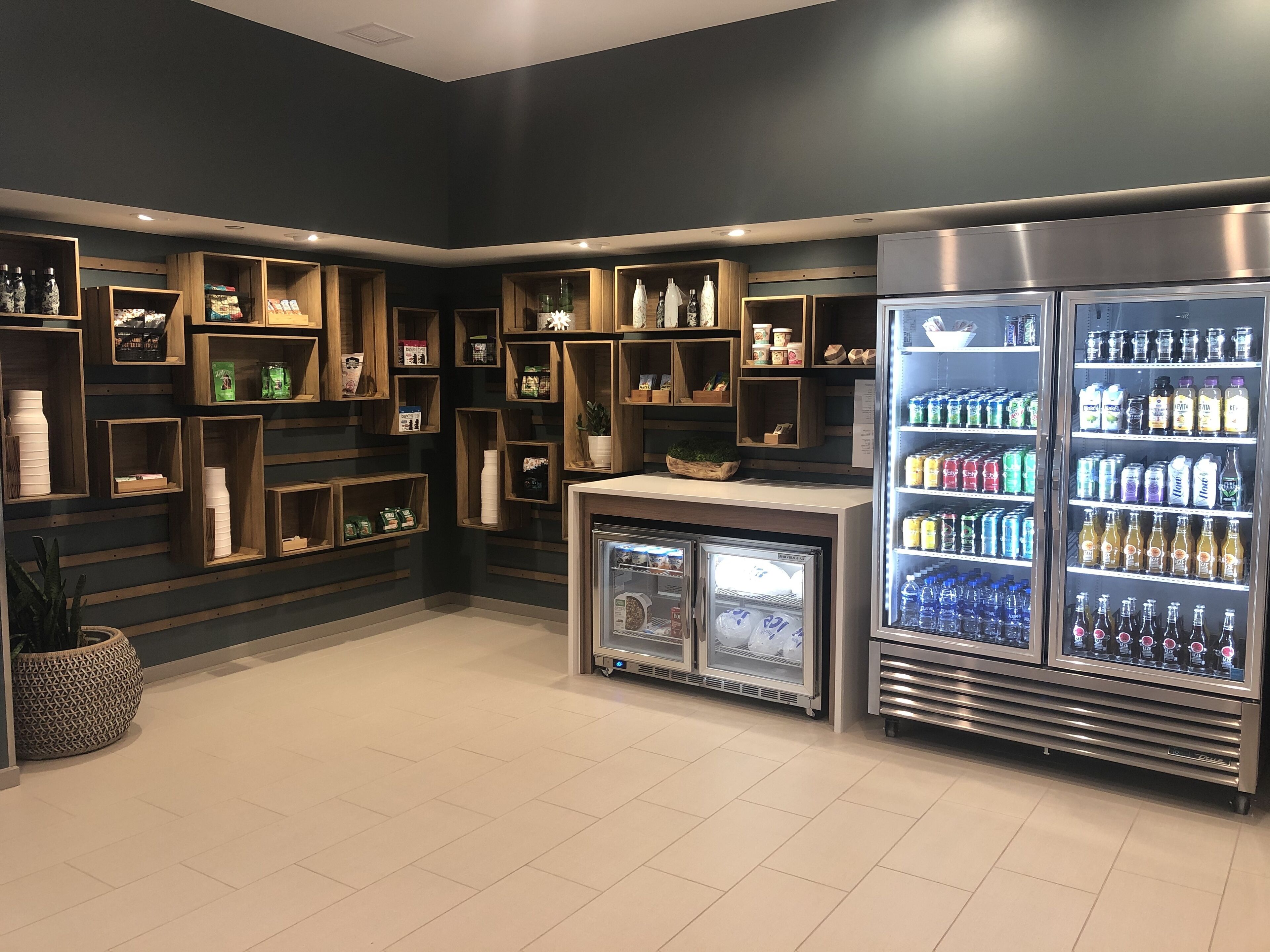 Um espaço comercial moderno com prateleiras de madeira exibindo diversos produtos, um refrigerador para alimentos e uma geladeira para bebidas.