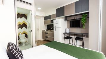 Quarto de hotel compacto com cama, pequena área de cozinha, banheiro e sala de jantar.