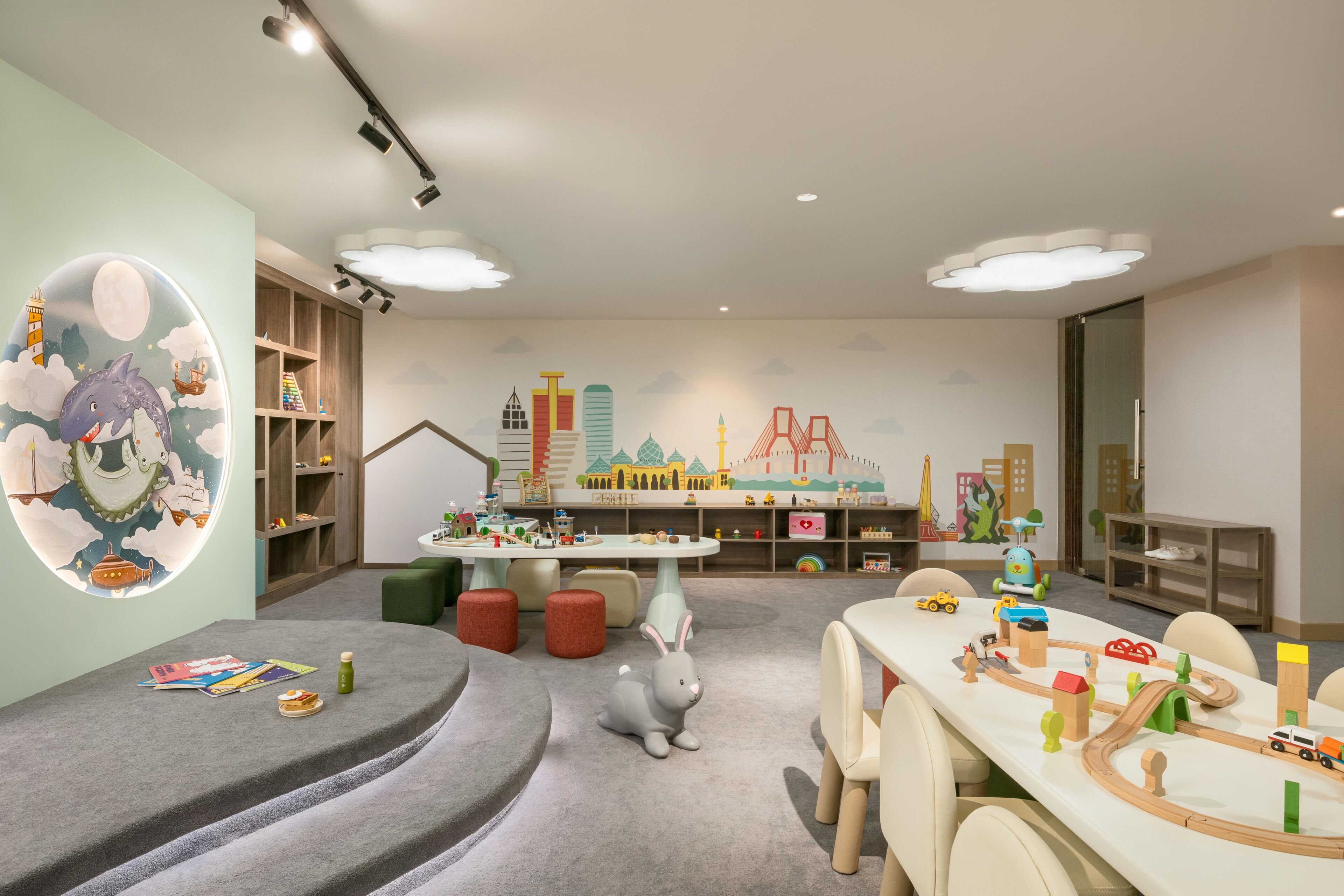 Uma sala de brinquedos infantil com um mural de paisagem urbana, uma mesa de brincar com brinquedos e um coelho de pelúcia.