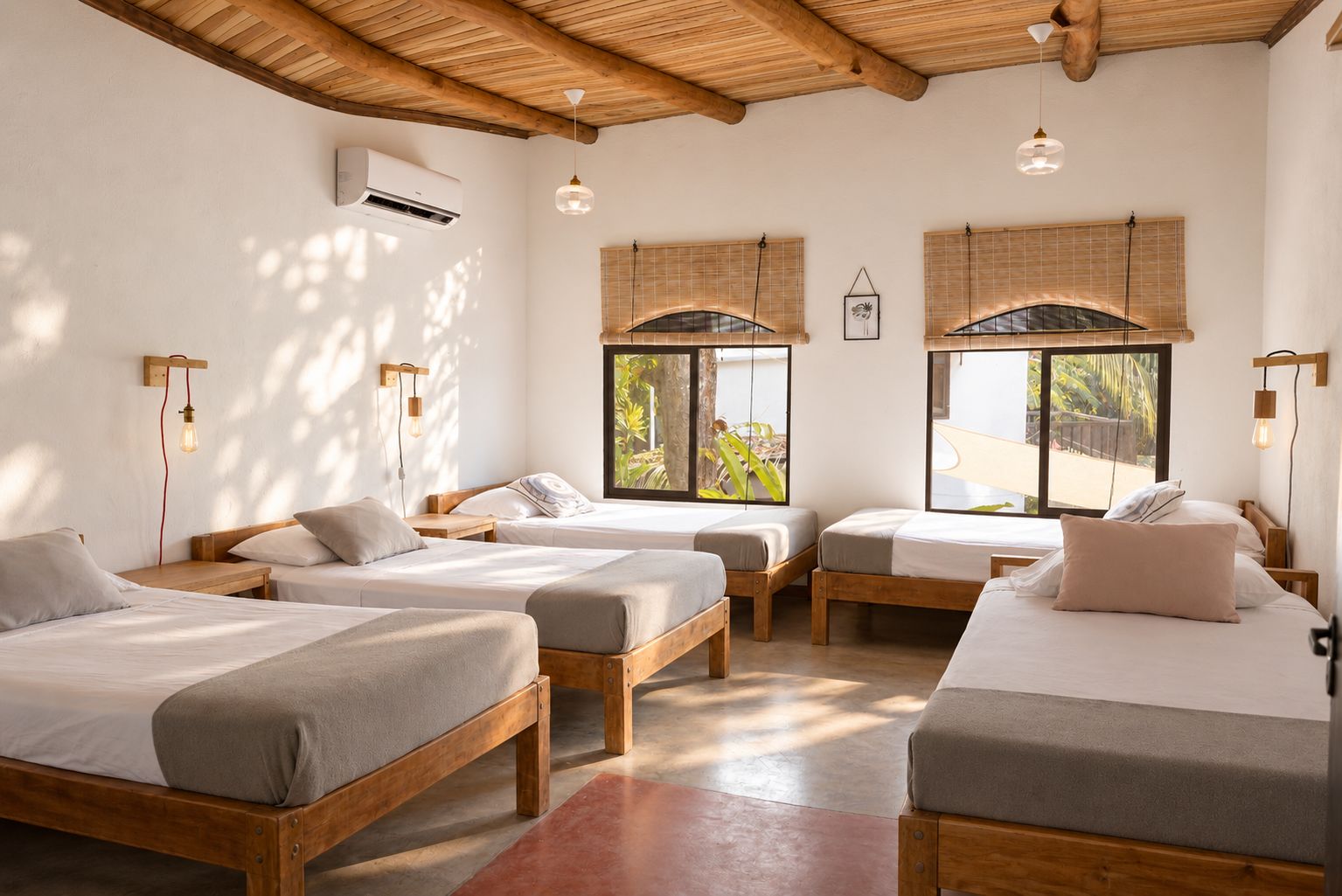 Quarto com quatro camas de madeira, um ventilador de teto e grandes janelas com persianas de bambu.