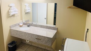 Um banheiro com pia de bancada de granito, espelho, porta-toalhas, lixeira e área de chuveiro.