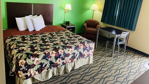 Quarto de hotel com cama grande, escrivaninha, cadeira, ventoinha no teto e parede verde.