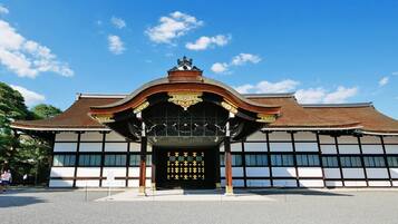 Um edifício japonês tradicional com telhado curvo, entrada decorativa e céu azul claro ao fundo.