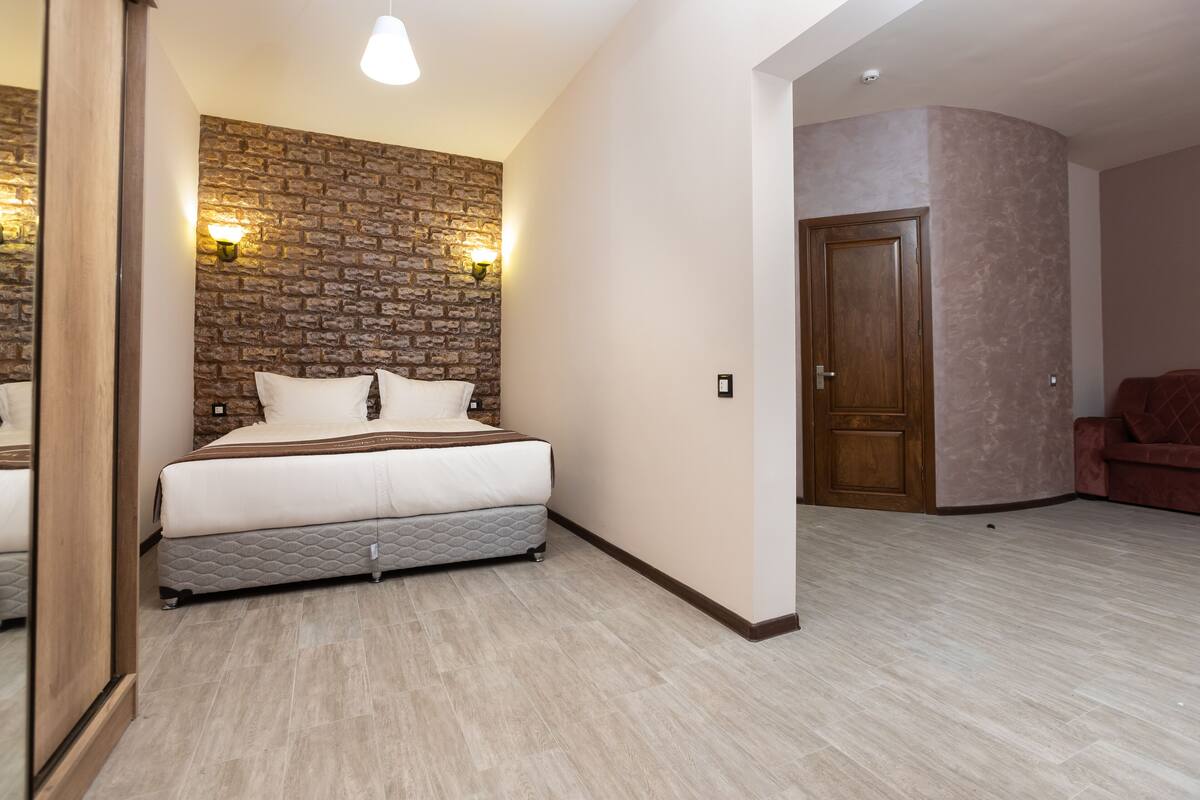 Quarto com parede de tijolos, cama com roupa de cama branca e porta de madeira.