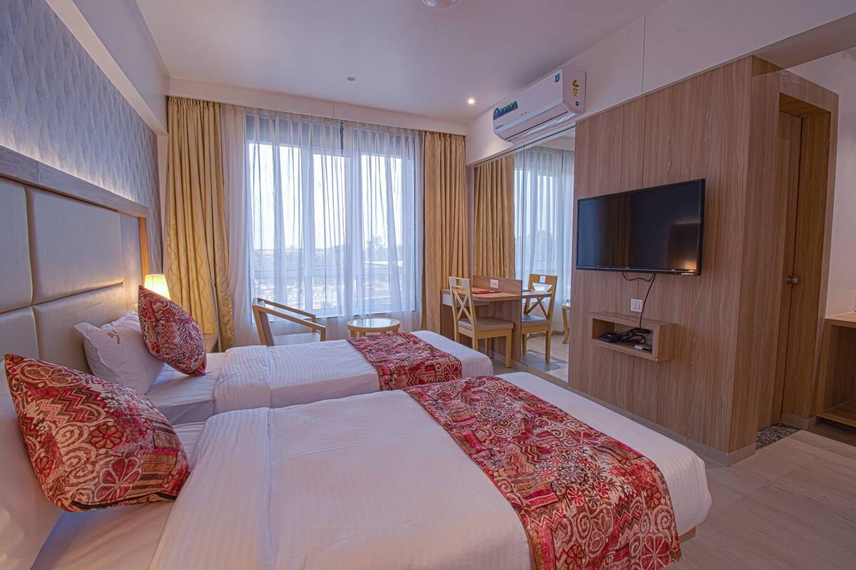 Quarto de hotel com duas camas, televisão, área de refeições e ar condicionado.