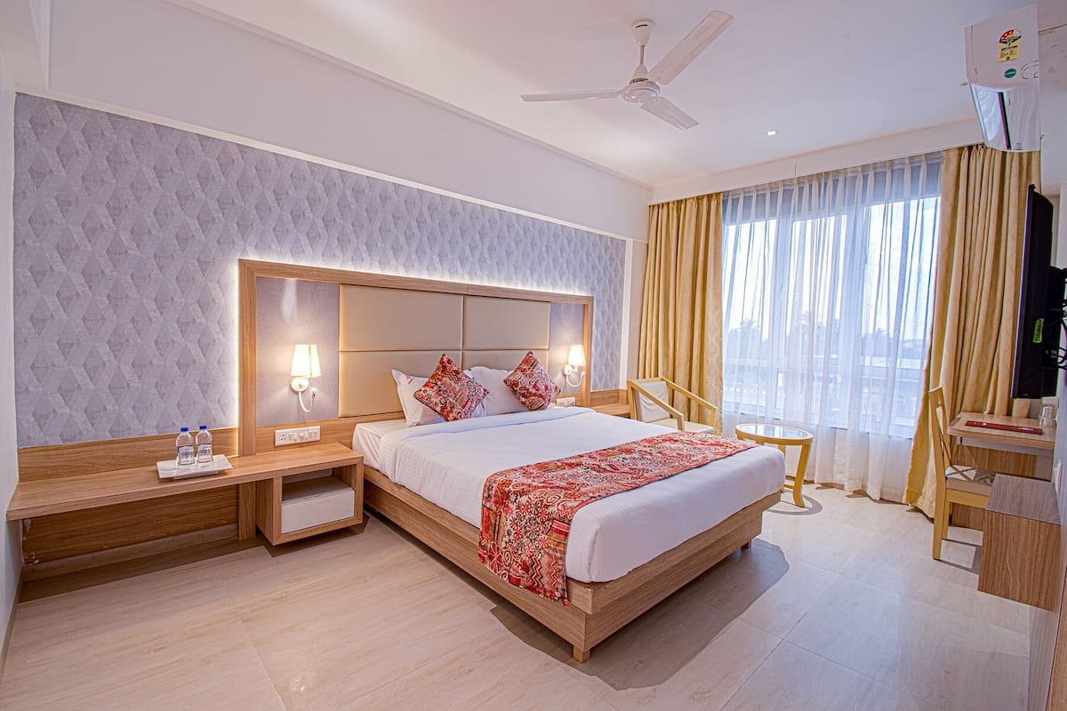 Quarto de hotel com uma cama grande, mesas de cabeceira, escrivaninha, cadeira, televisão e ventoinha no teto.