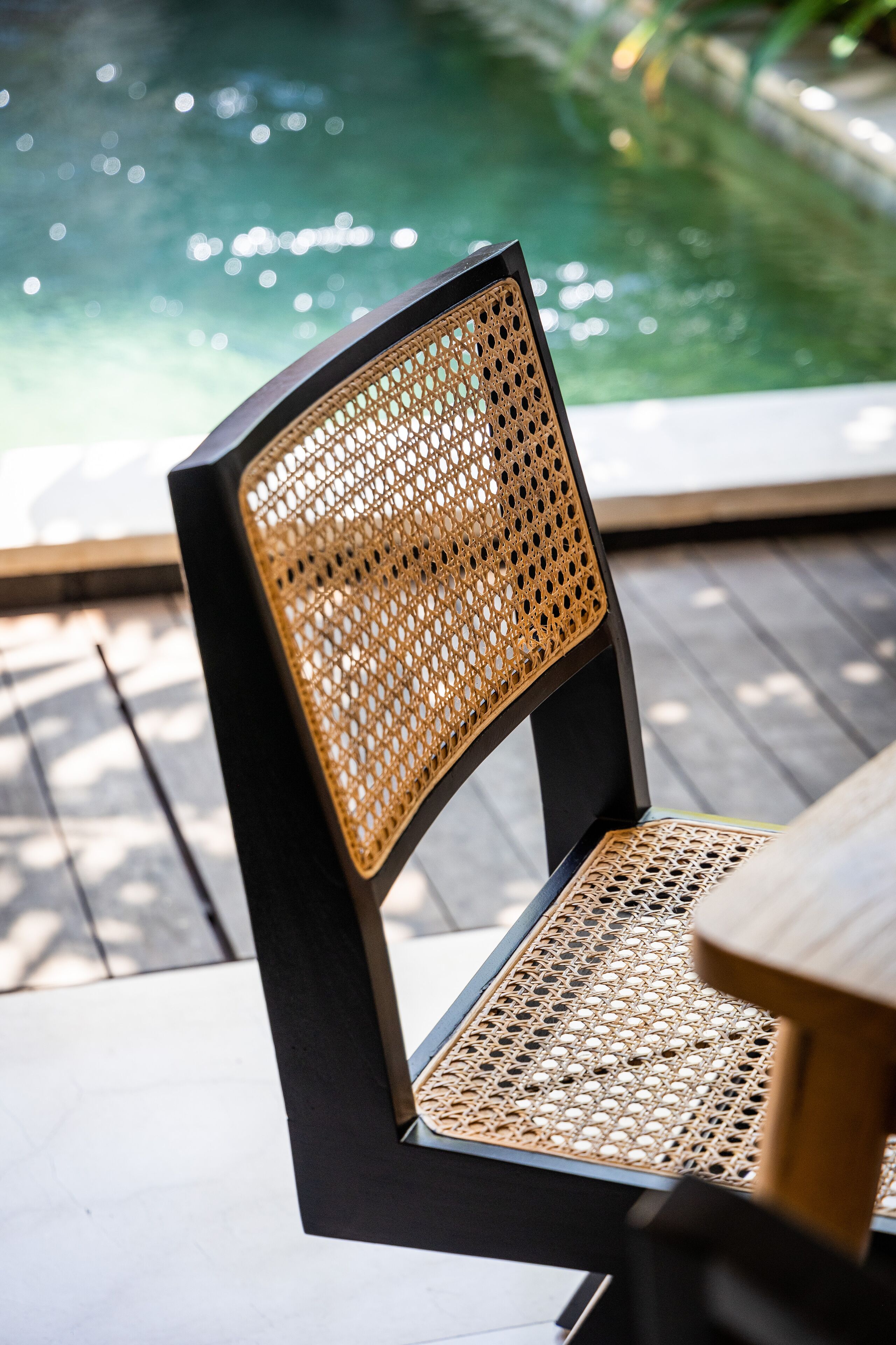 Uma cadeira de vime com estrutura preta, colocada perto de uma mesa à beira da piscina.