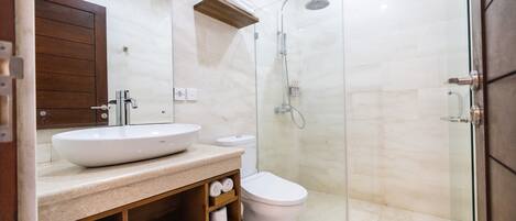 Uma casa de banho moderna com uma grande pia branca, uma sanita e uma área de duche com parede de vidro.