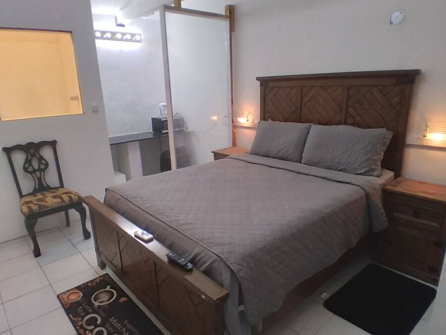 Quarto com cama, mesas de cabeceira, uma cadeira, escrivaninha e espelho.
