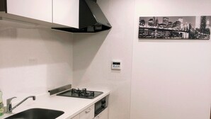 Cozinha compacta com armários brancos, uma pia de aço inoxidável, fogão e coifa preta. Há uma fotografia em preto e branco da paisagem urbana na parede e piso de madeira.