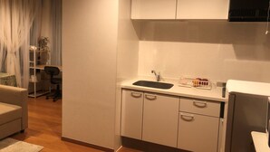 Uma cozinha compacta com pia, armários e micro-ondas. Há uma cadeira e uma mesa pequena com um vaso de flores.