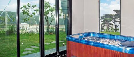 Uma casa de banho moderna com uma ampla janela de vidro, uma banheira de hidromassagem e vista para uma paisagem verde.