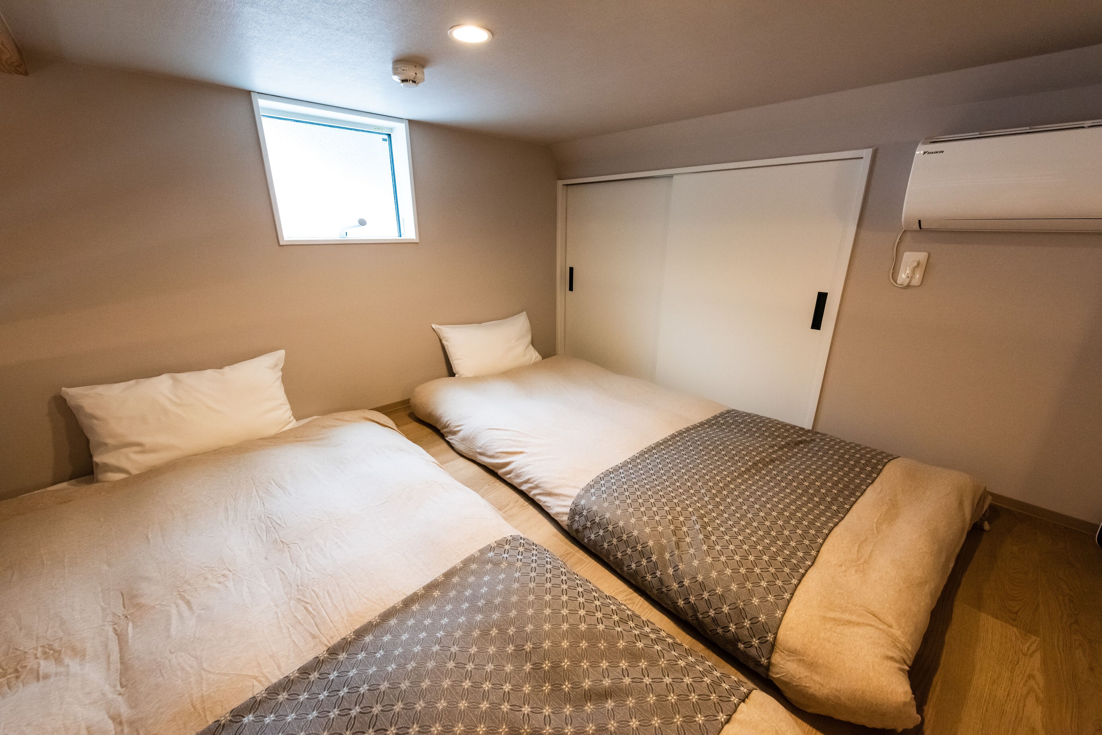 Quarto com duas camas, uma janela e ar condicionado.