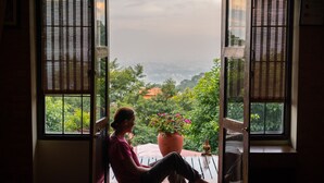 Uma pessoa sentada perto de uma janela, com vista para vegetação e uma estátua de Buda.
